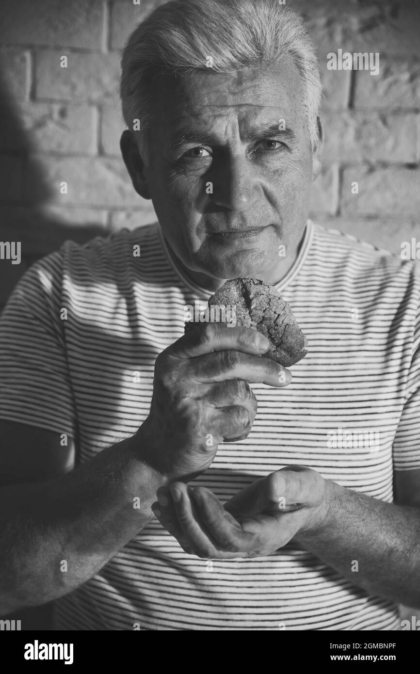 Poor man with little piece of bread on brick wall background. Black and ...