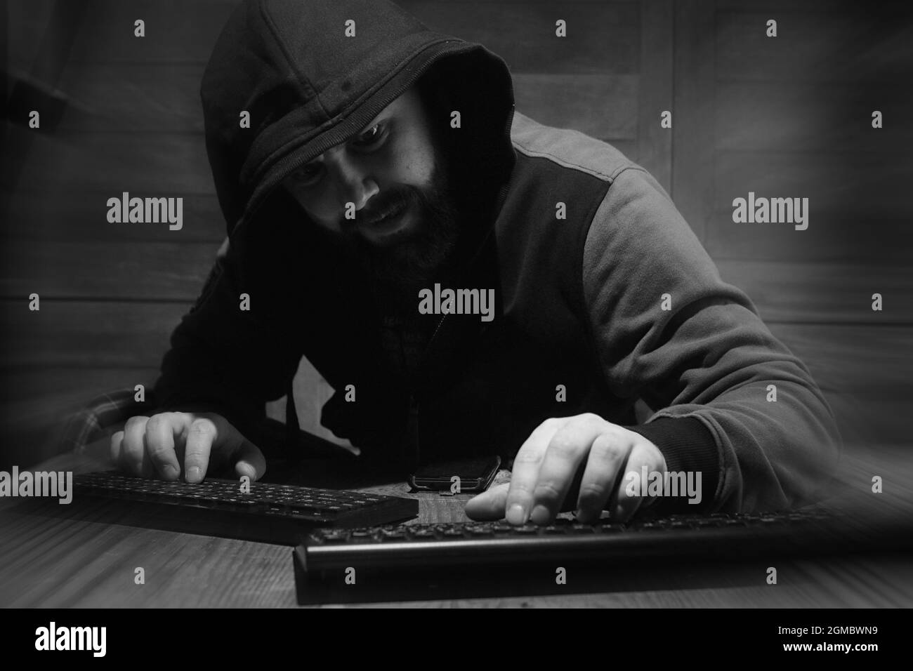 The hacker in the hood sits and works behind the computer Stock Photo ...