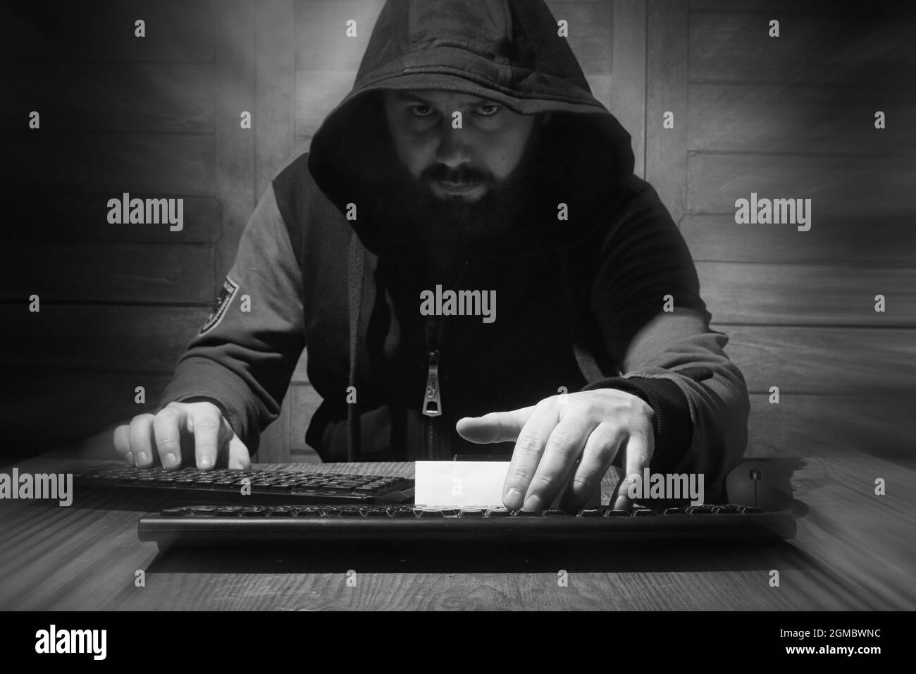 The hacker in the hood sits and works behind the computer Stock Photo ...