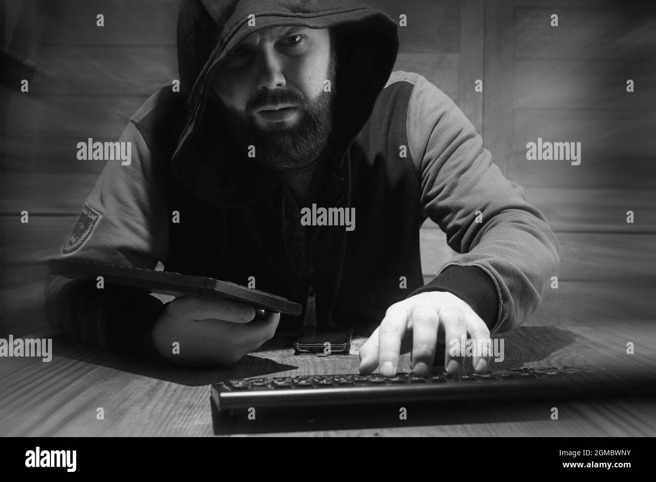 The hacker in the hood sits and works behind the computer Stock Photo ...