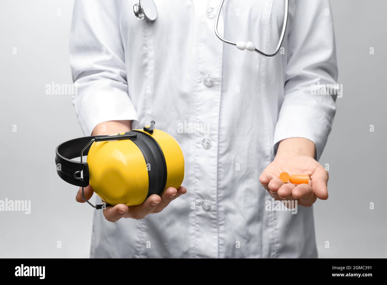 Female doctor holding headphones and earplugs on light background ...