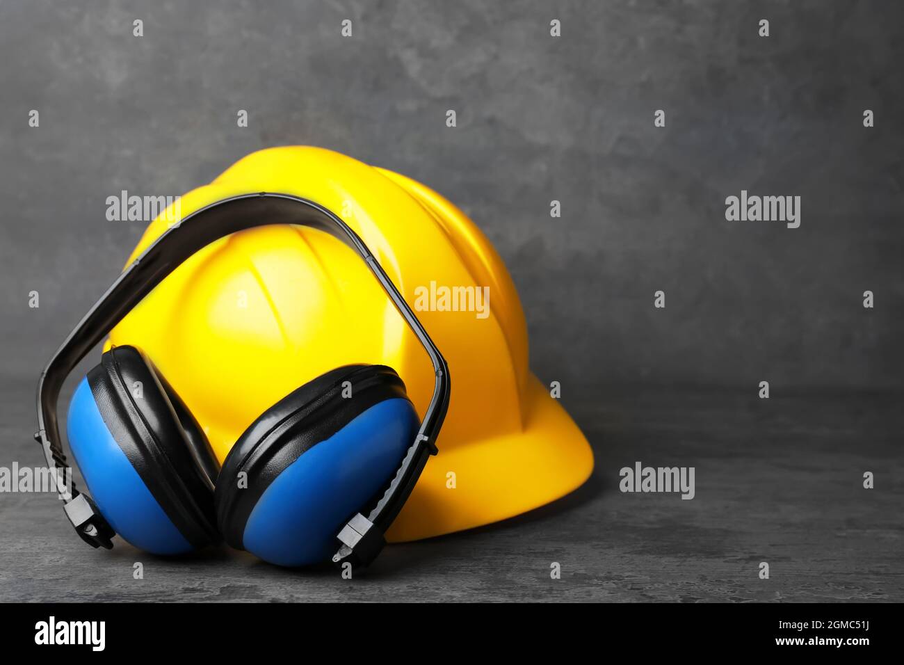 Headphones and hard hat on table against grey background. Hearing ...