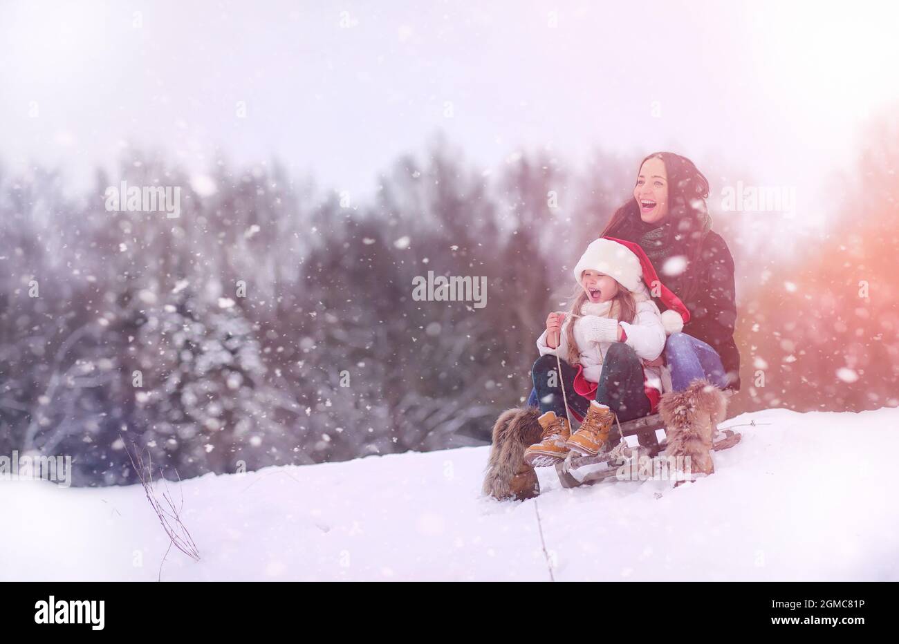 Winter fairy tale, a young mother and her daughter ride a sled in the ...