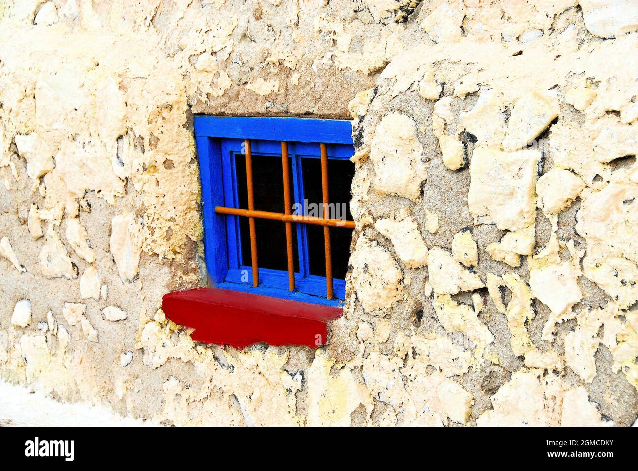A colorful window frame of blue and red in a stone wall of beige and ...