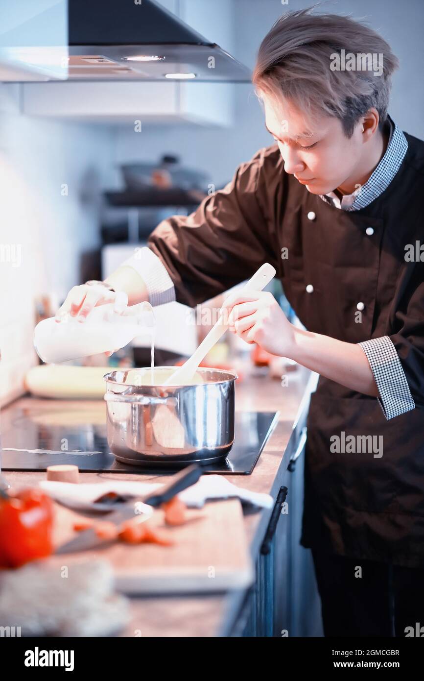 A young Asian cook in the kitchen prepares food in a cook suit Stock ...