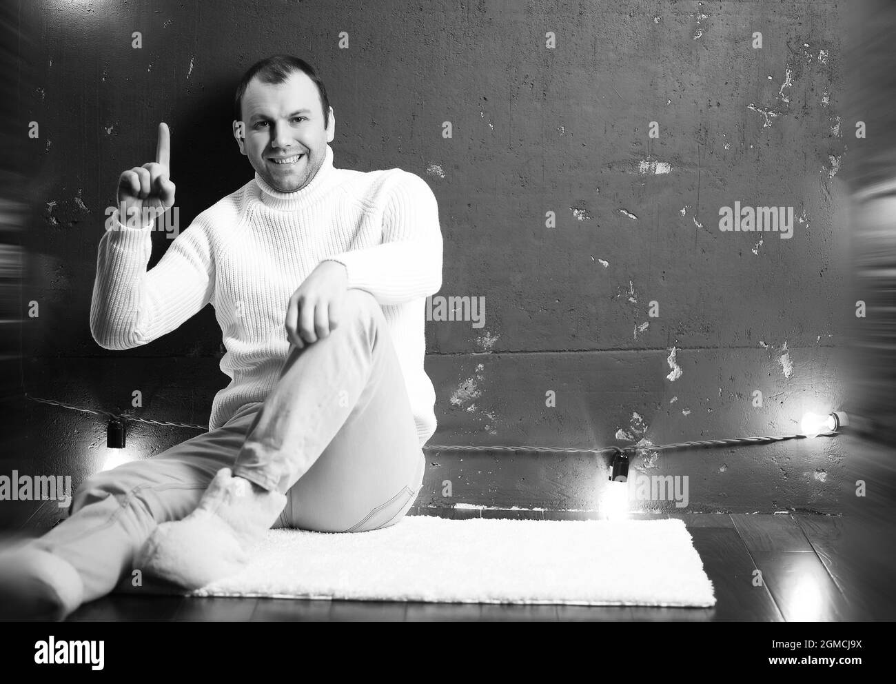 A man in a white sweater in a dark room listening to music Stock Photo ...