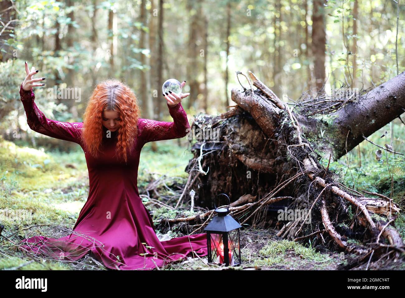 The red-haired witch holds a ritual with a crystal ball in the forest ...