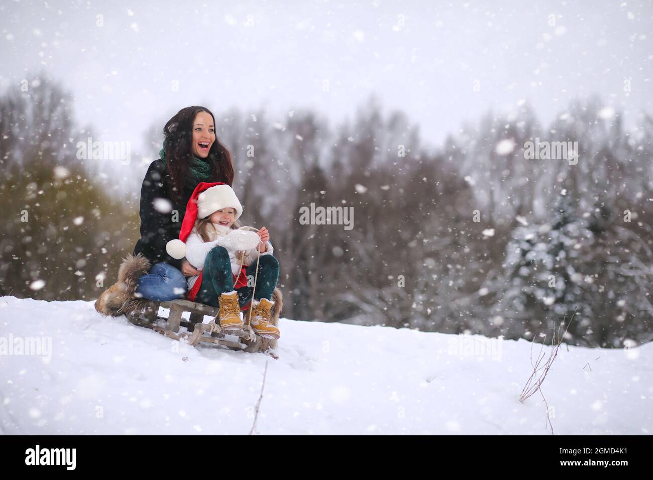 Winter fairy tale, a young mother and her daughter ride a sled in the ...