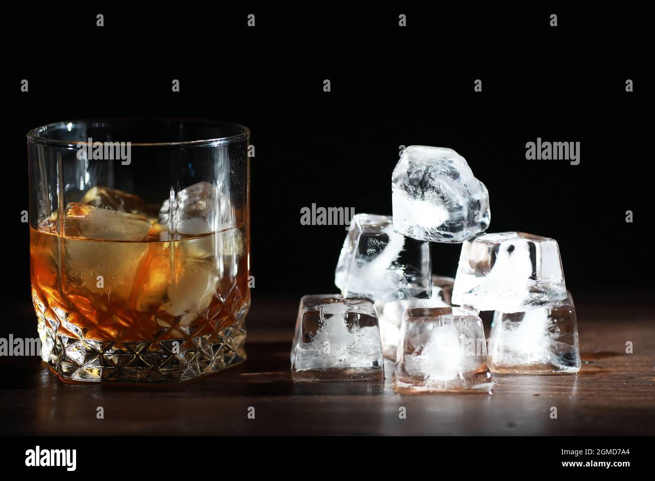 A glass of strong alcoholic drink with ice on wooden bar counter ...