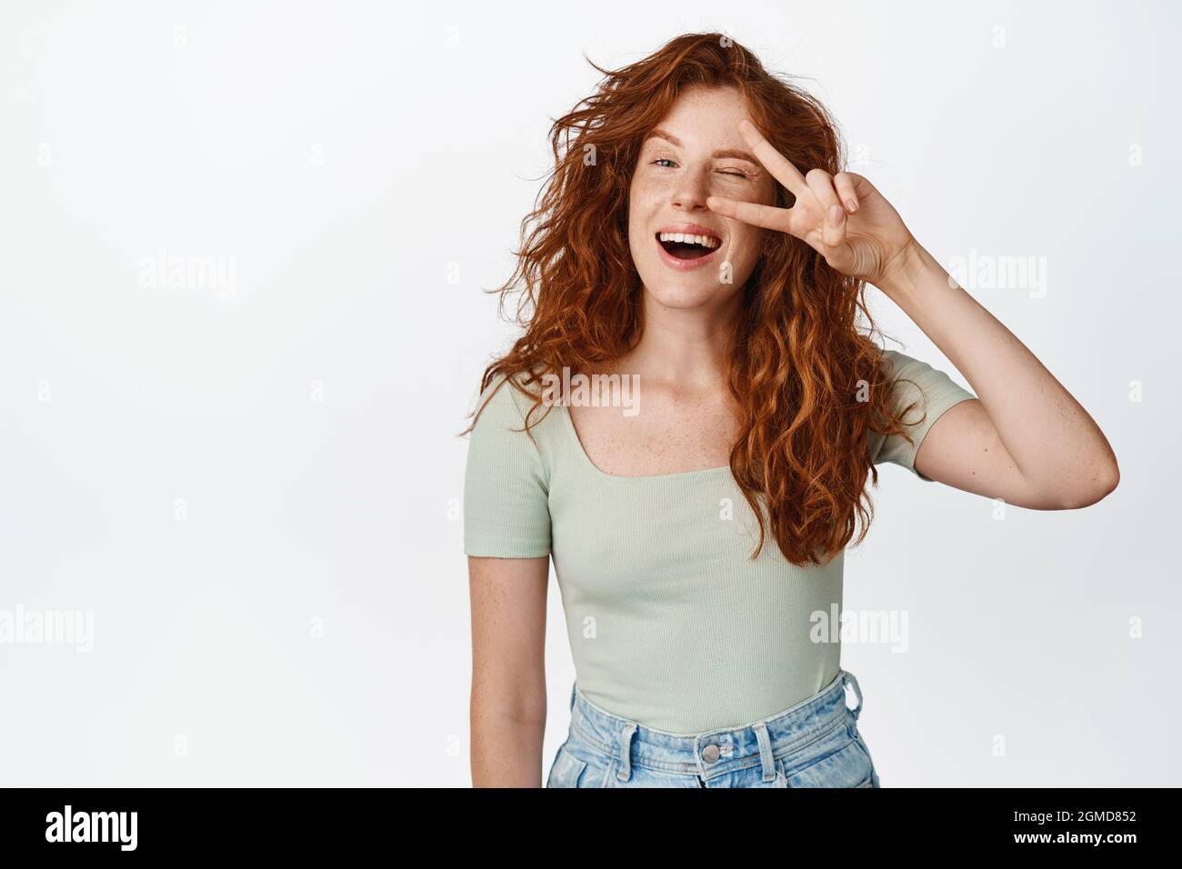 Positive redhead girl shows peace salute sign, winking and smiling at ...