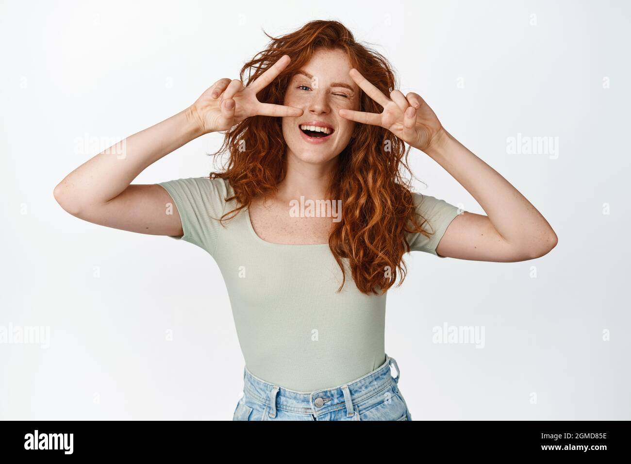 Happy redhead woman shows peace signs near face, winking and smiling ...