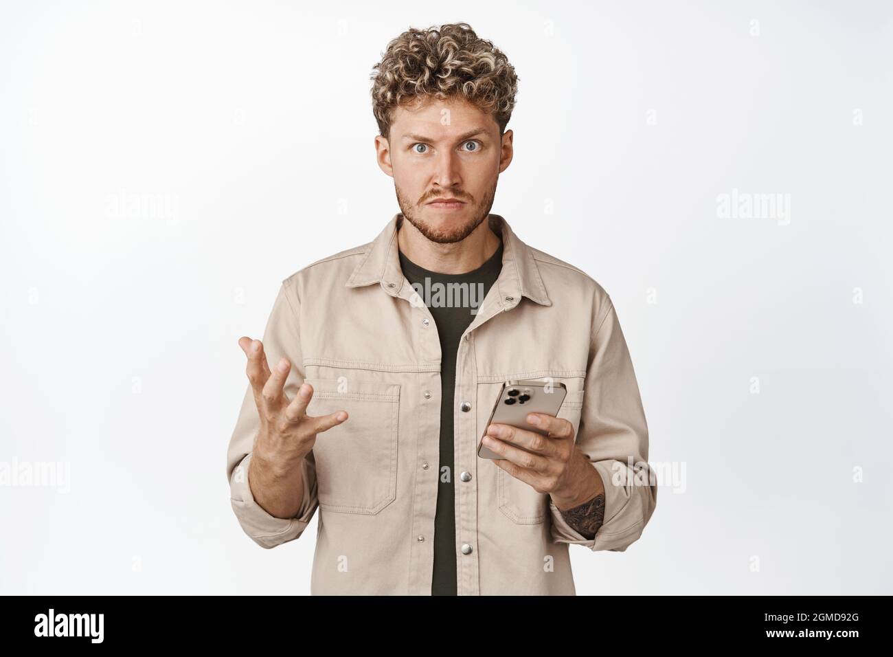 Annoyed and angry young man holding mobile phone, looking pissed-off at ...