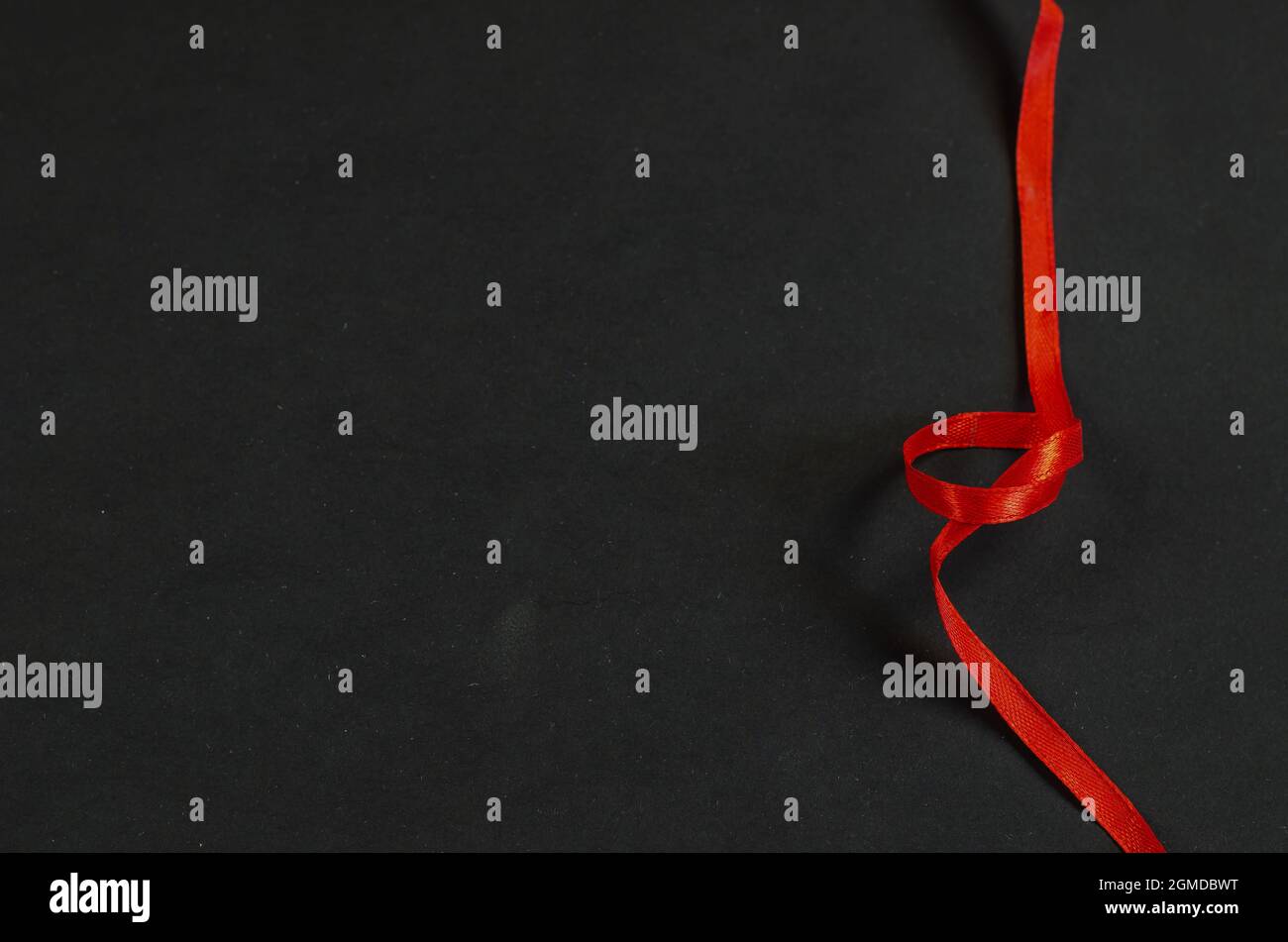 Red ribbon on a black background. Thin ribbon with tied knot. Co Stock ...