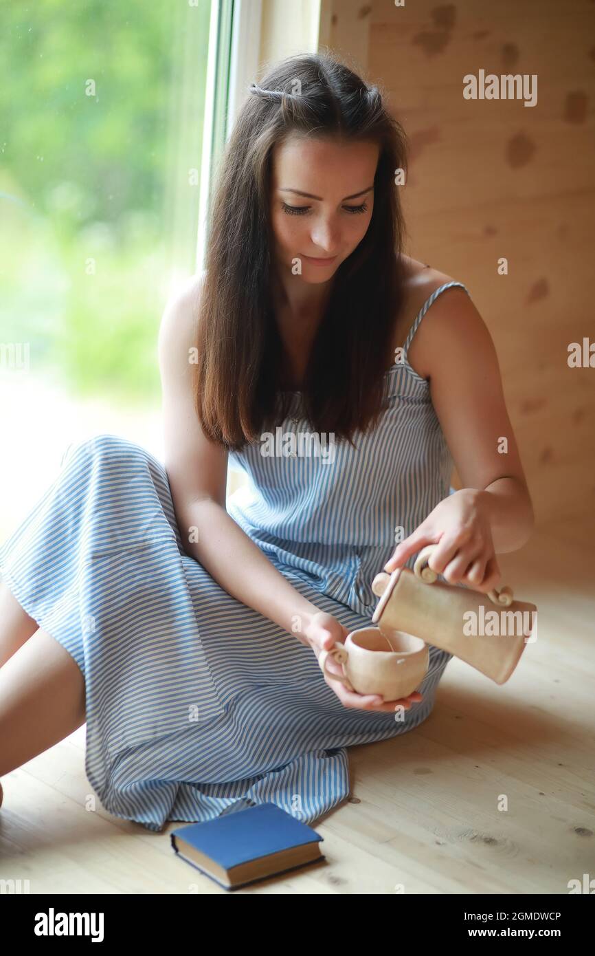 A girl at the window in the house reads a book and drinks tea Stock ...