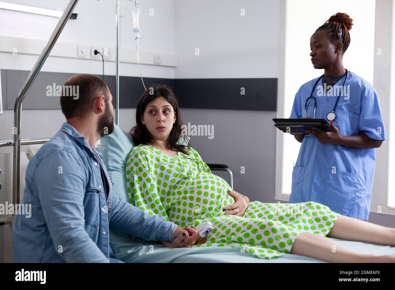 Young couple expecting child in hospital ward while talking to african ...