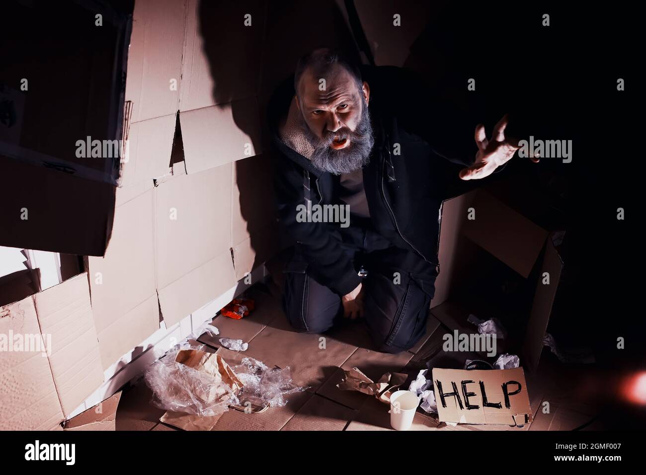 A homeless bearded man sits on boxes on street and asks for help. Need ...