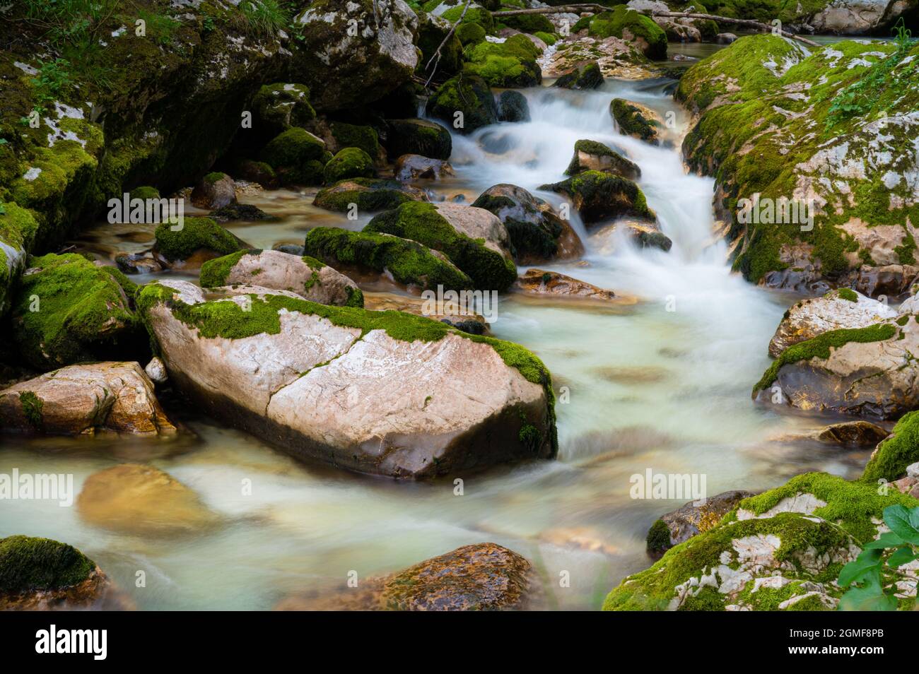 Blurred image of beautiful stream of water flowing over mossy rocks in ...