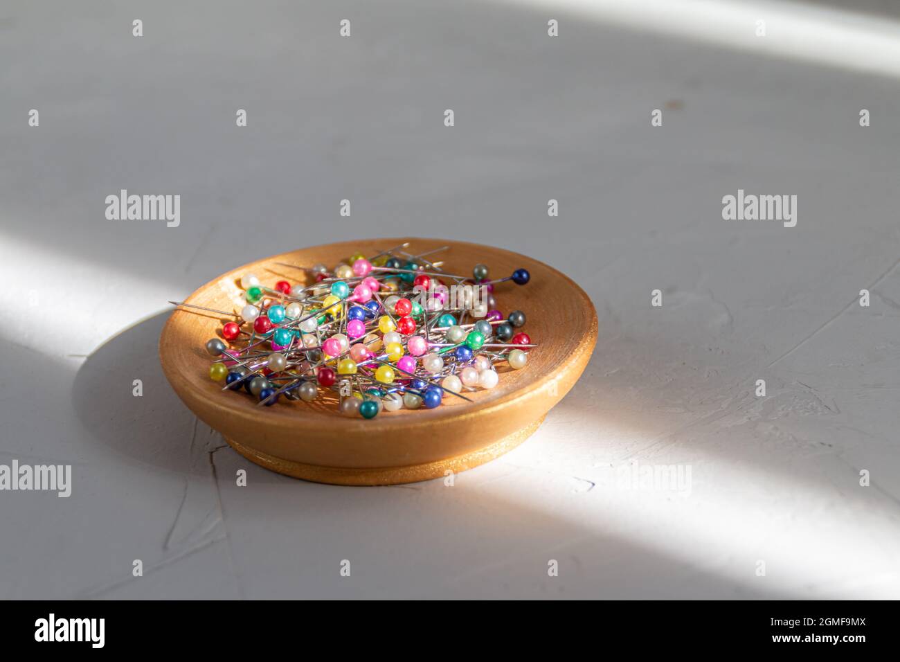 colored sewing pins in a golden plate against grey background with ...
