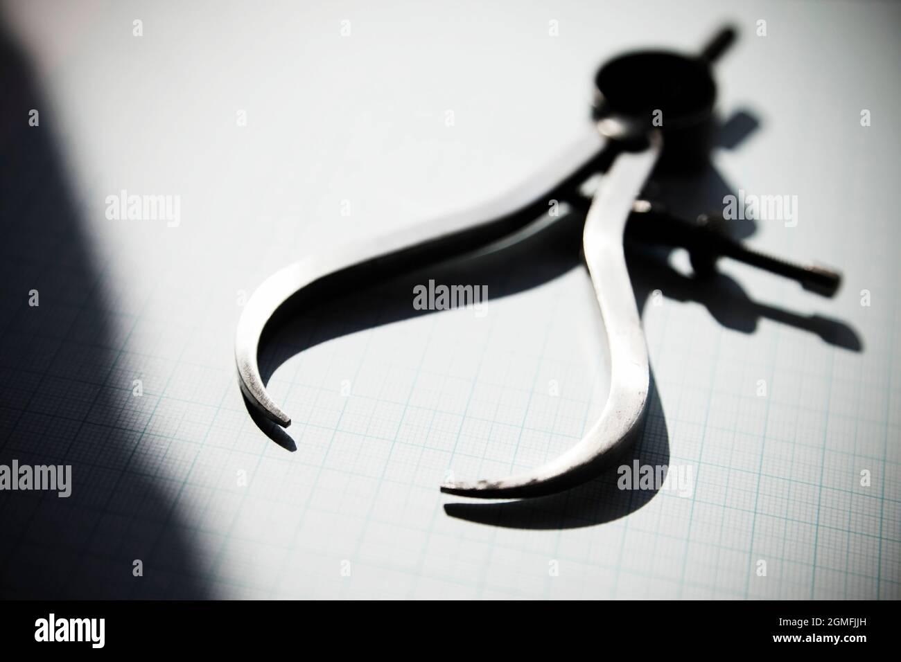 Metal outside spring calipers casting abstract shadow on piece of graph ...