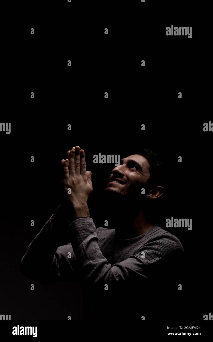 Headshot of serious confident young man praying in dark room. Lit from ...