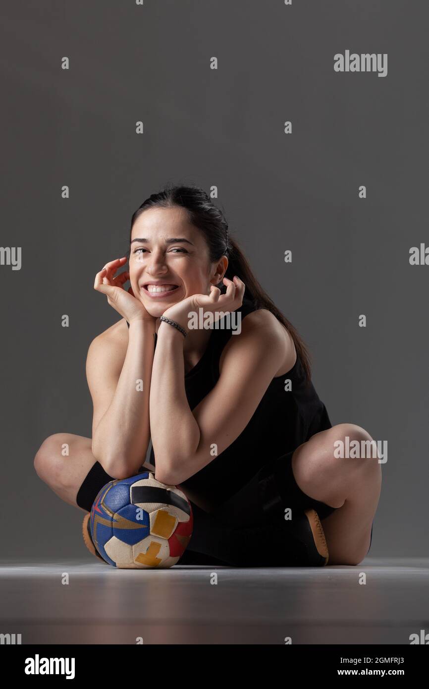 Handball player sitting on the ground. Girl posing with ball and making ...