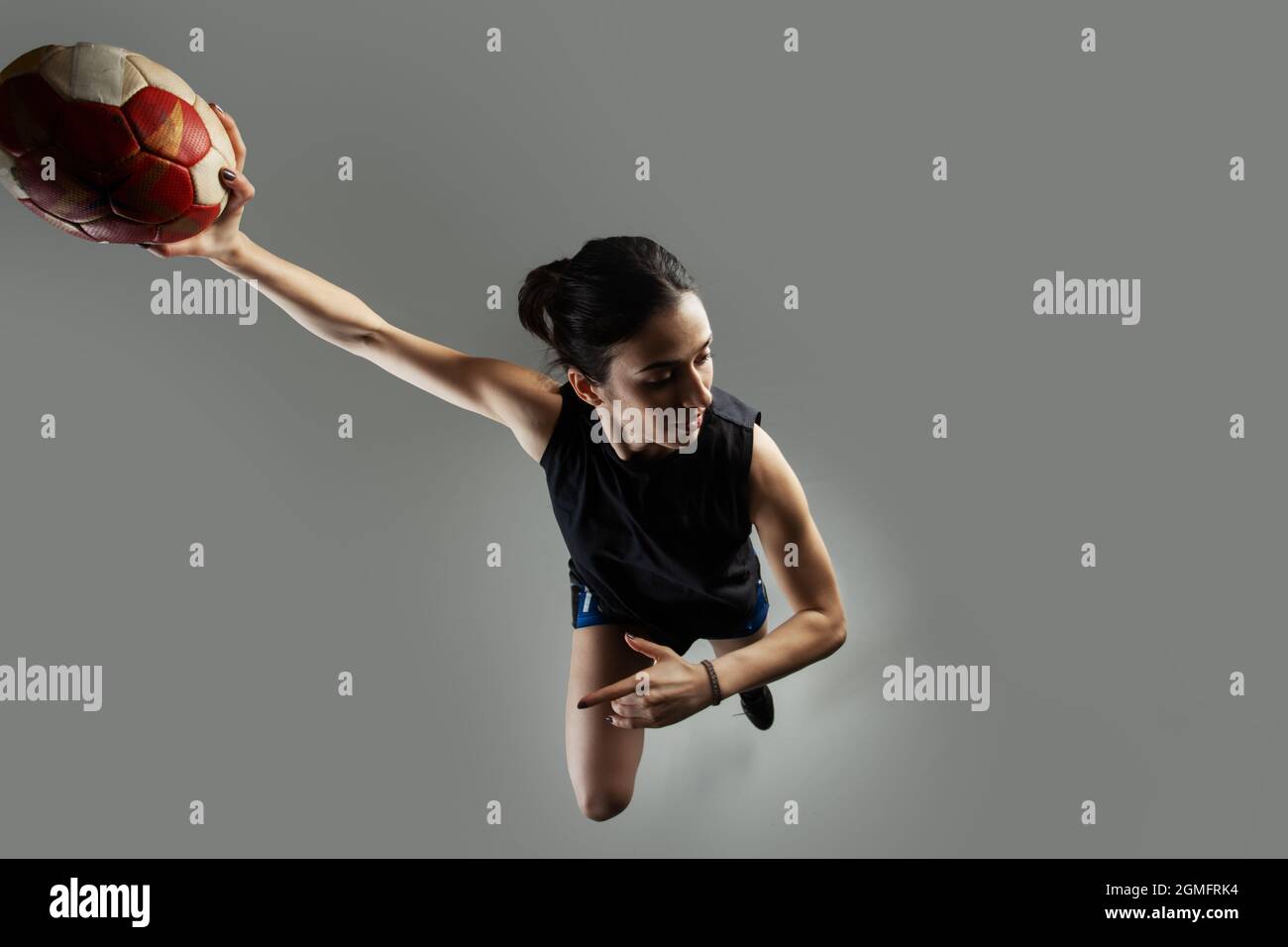 Handball player posing on light gray background. Girl jumping with ball ...