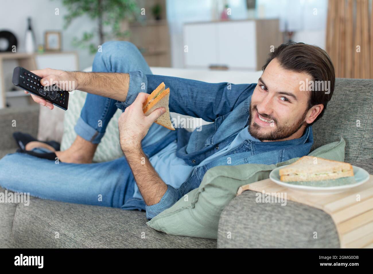 man changing tv channel with remote control while eating sandwich Stock ...