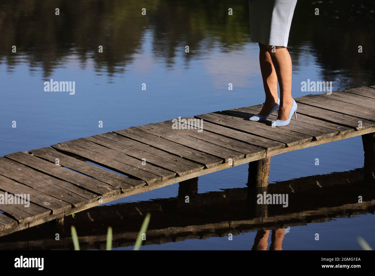 cropped photo of female legs walking on a wooden pier on the river ...