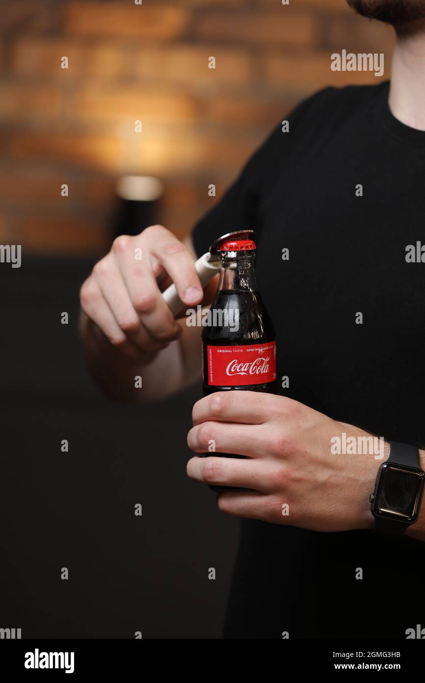 RIVNE, UKRAINE JUNE 26 2020: a young man opening a glass bottle of coca ...