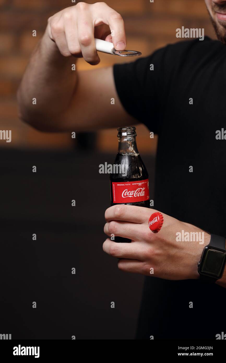 RIVNE, UKRAINE JUNE 26 2020: a young man opening a glass bottle of coca ...