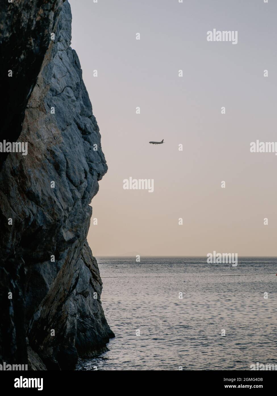 Vertical shot of a big cliff in the sea and an airplane in the sky ...