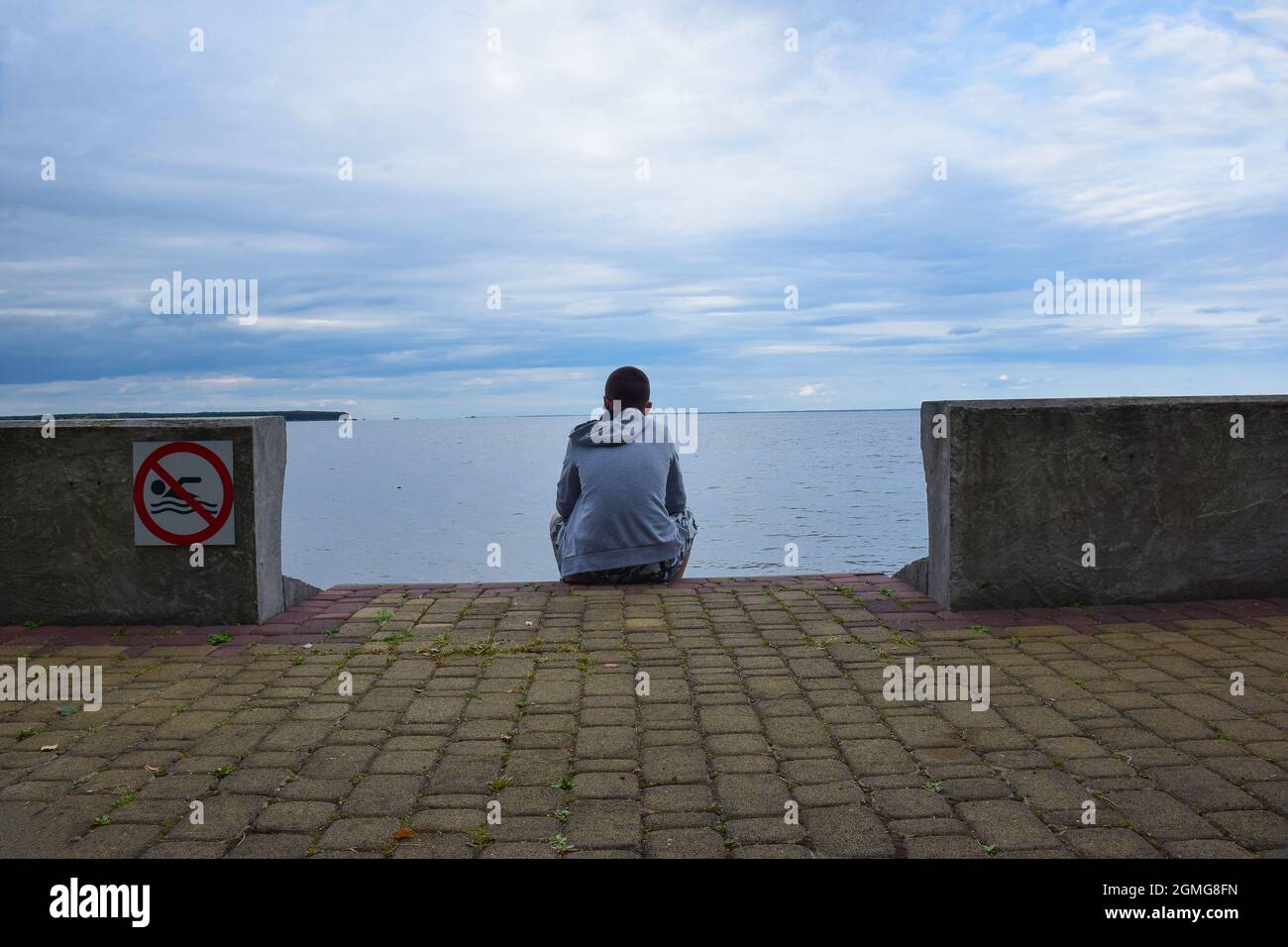 A young guy sits with his back on the embankment, on the seashore. The ...