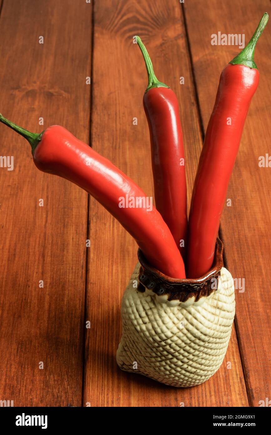 Three red fresh chili pepper pods inserted vertically into a small vase ...