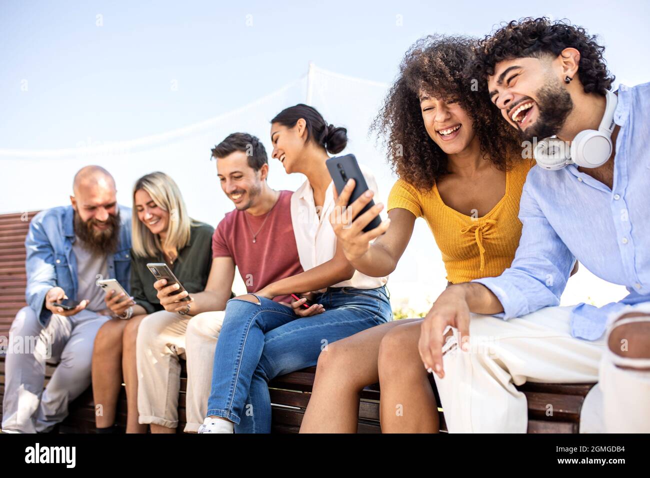 Diverse group of happy college friends using mobile phone while sitting ...
