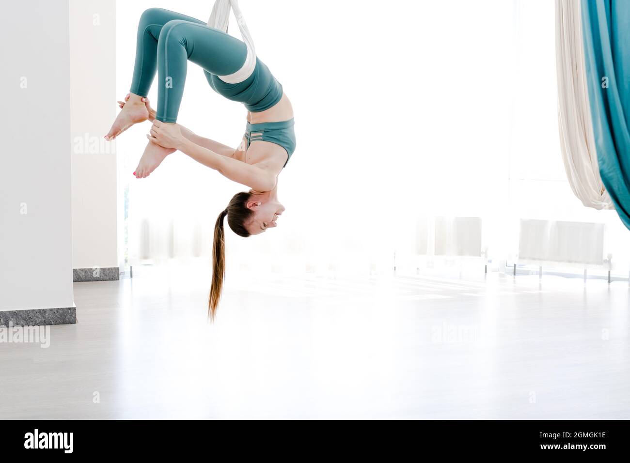 sportswoman hanging in a hammock in an inverted position on a white ...