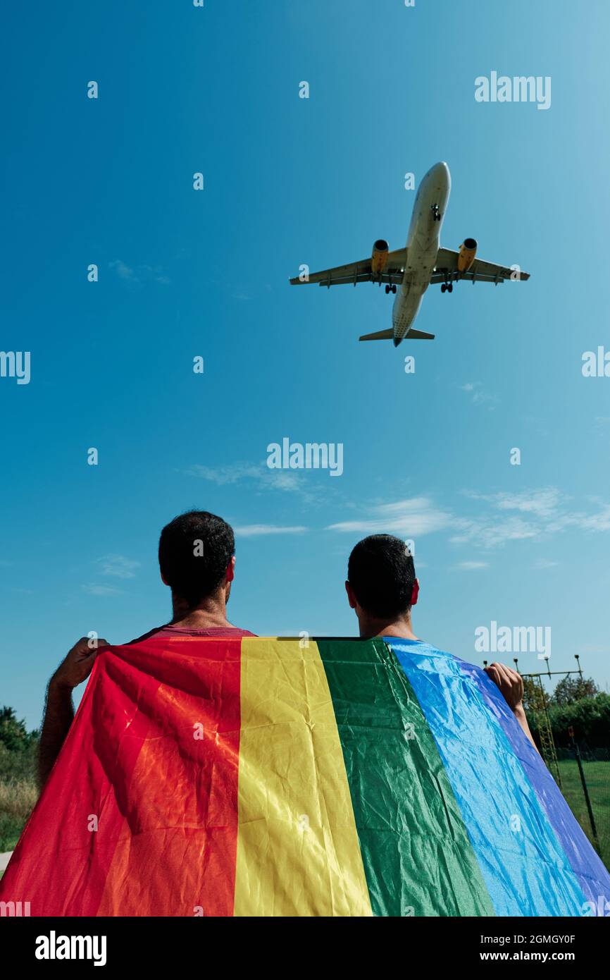 two homosexual men with gay flag looking to an airplane Stock Photo - Alamy