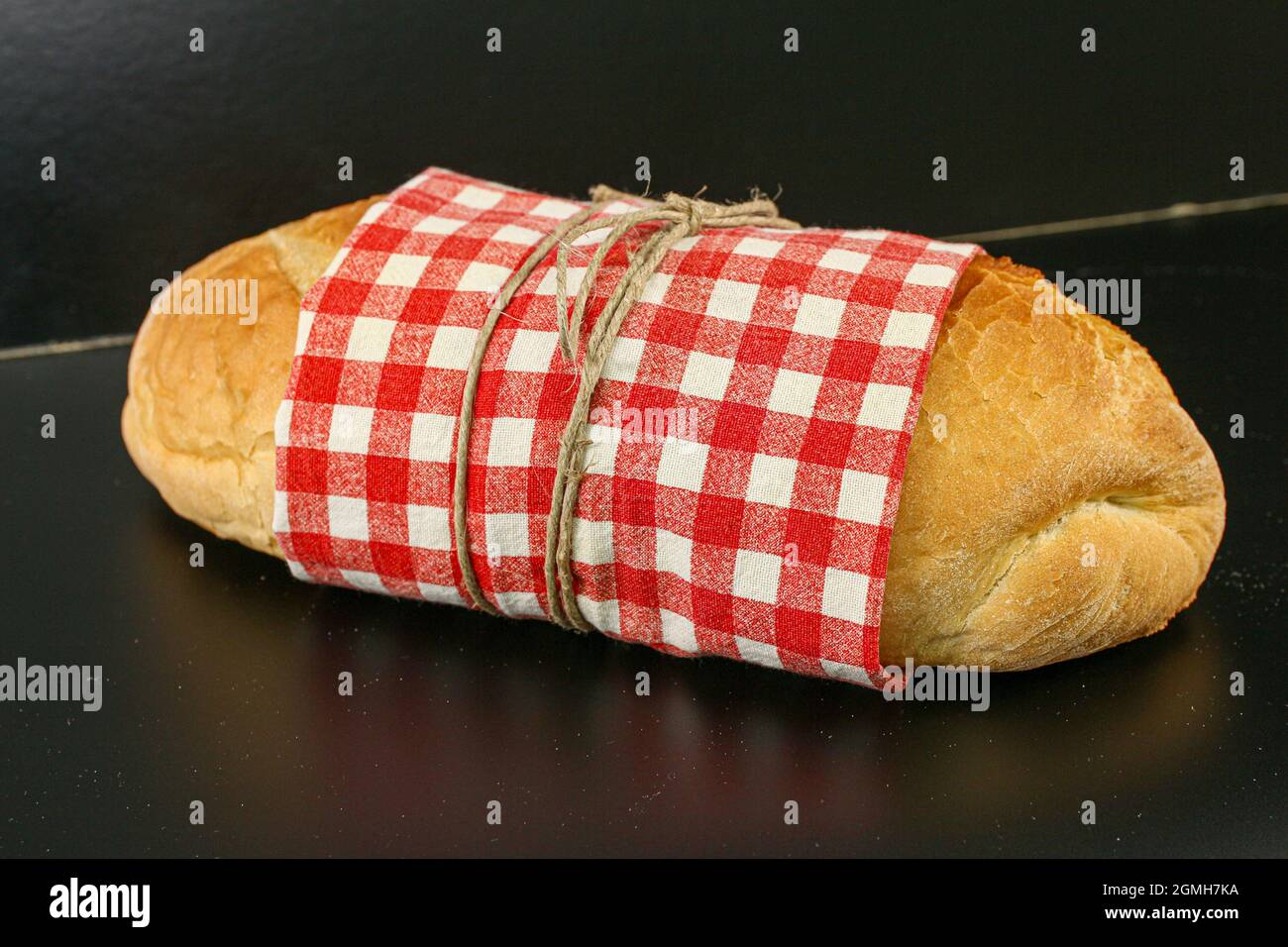 A loaf of bread wrapped with red checkered cloth and burlap ribbon ...