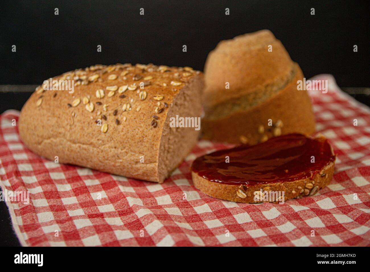A loaf of bread topped with strawberry jam on a red checkered cloth ...