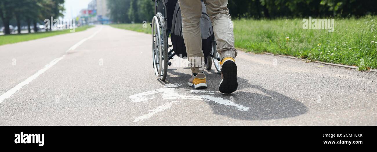 Man helping disabled person in wheelchair to walk on sidewalk Stock ...