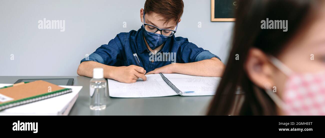 Boy with face mask writing at school Stock Photo - Alamy