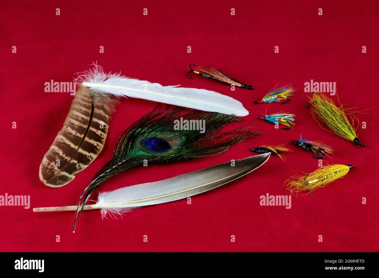 Assorted fly tying feathers and fishing flies on a red table top Stock ...