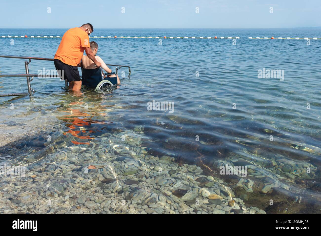 Disabled man on a wheelchair being transported into sea for swimming ...