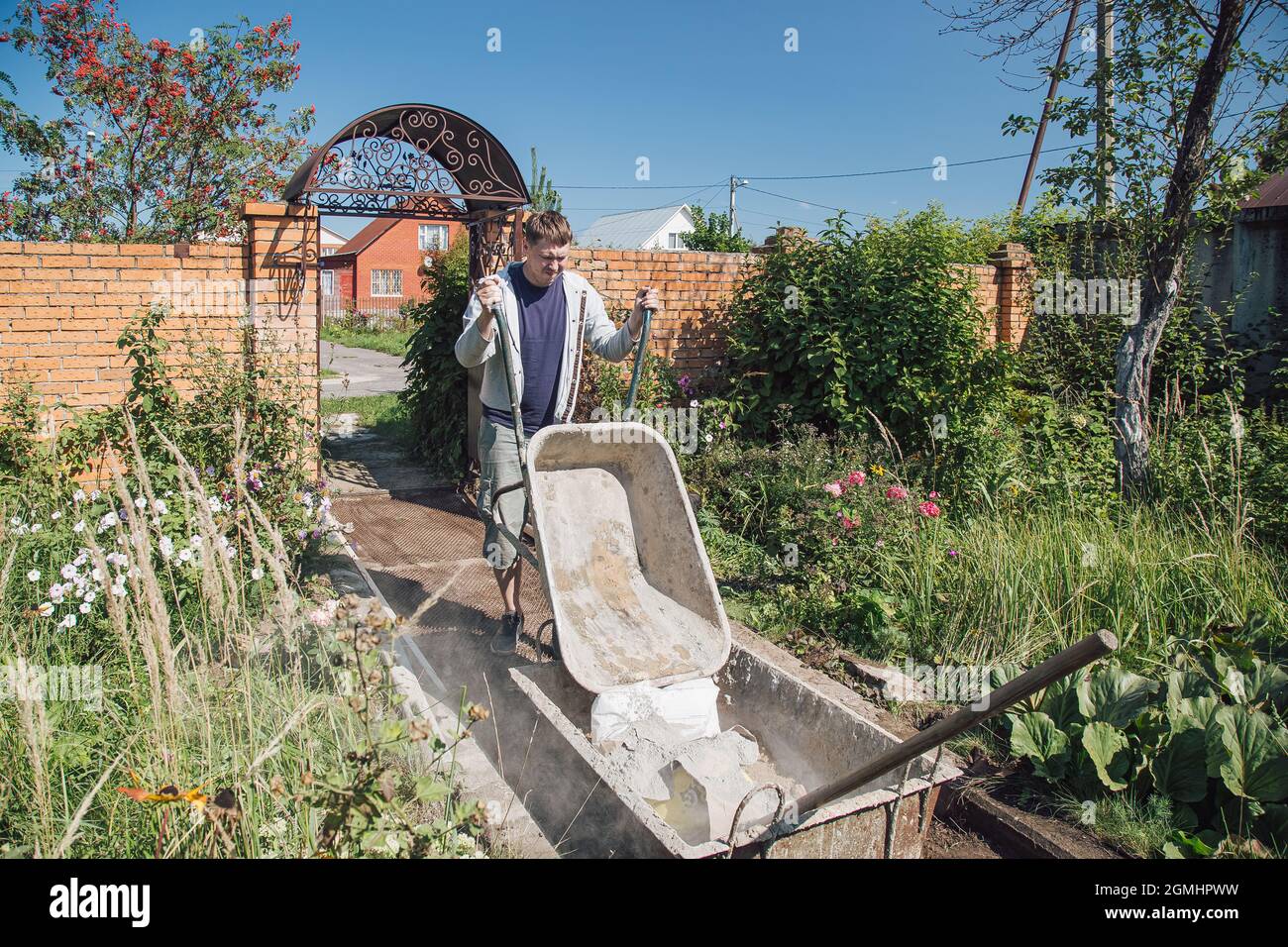A man unloads sand into a cement mixture for pouring a garden path ...