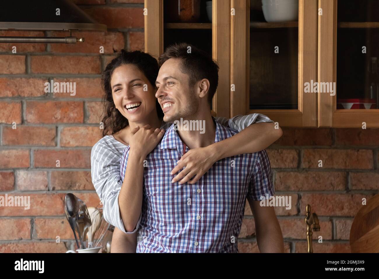 Happy beautiful latin woman cuddling from back sincere smiling husband ...