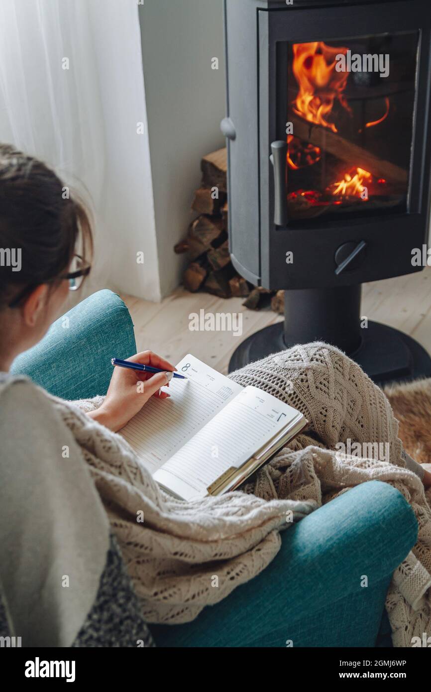 Young woman write in notebook sitting in armchair by fireplace Stock ...