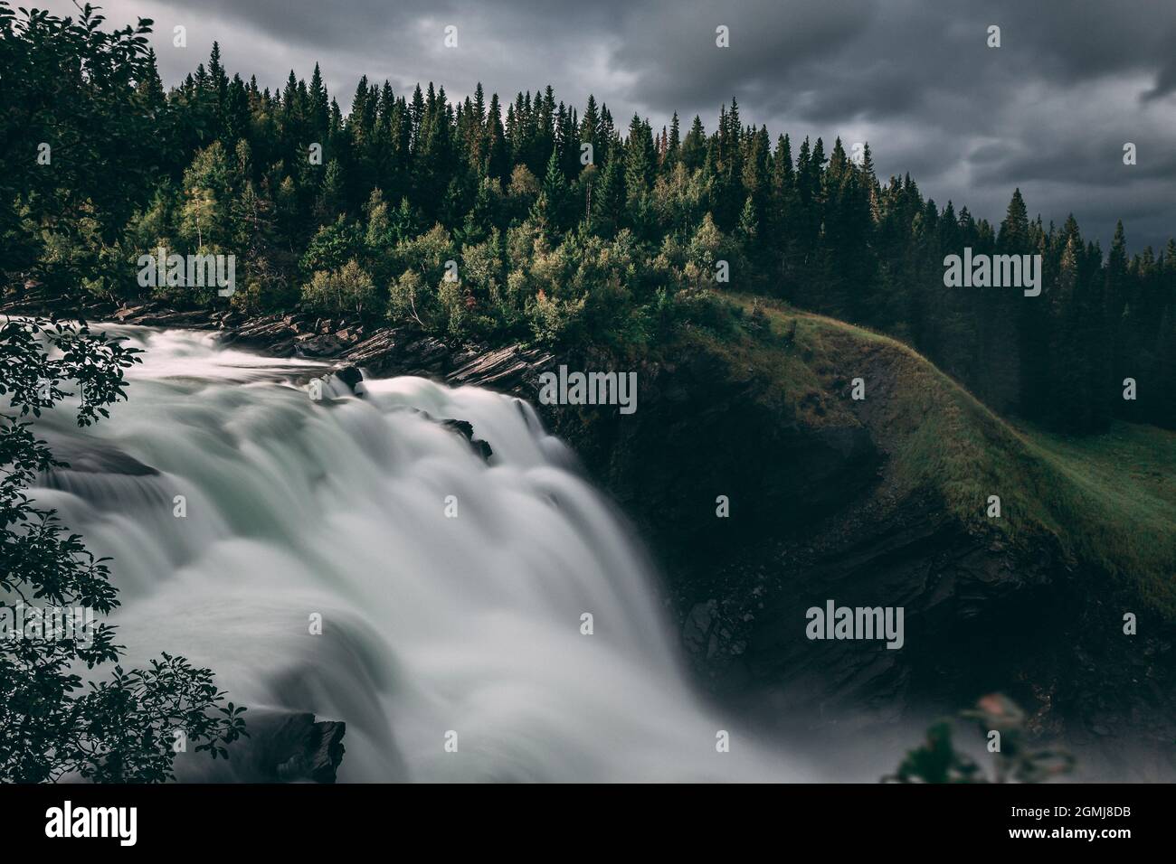 A beautiful waterfall surrounded with dense green trees under a gloomy ...