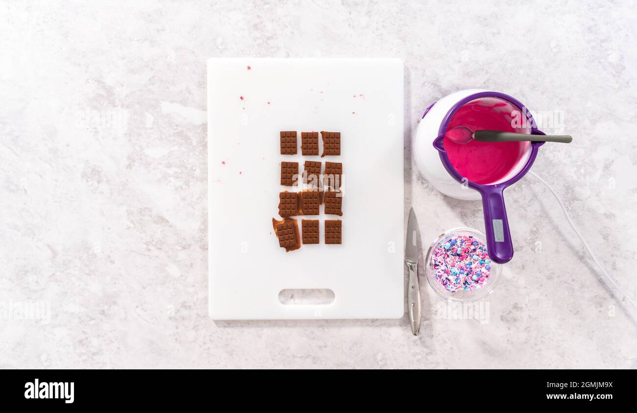 Flat lay. Drizzling melted pink chocolate on top of the mini chocolates ...