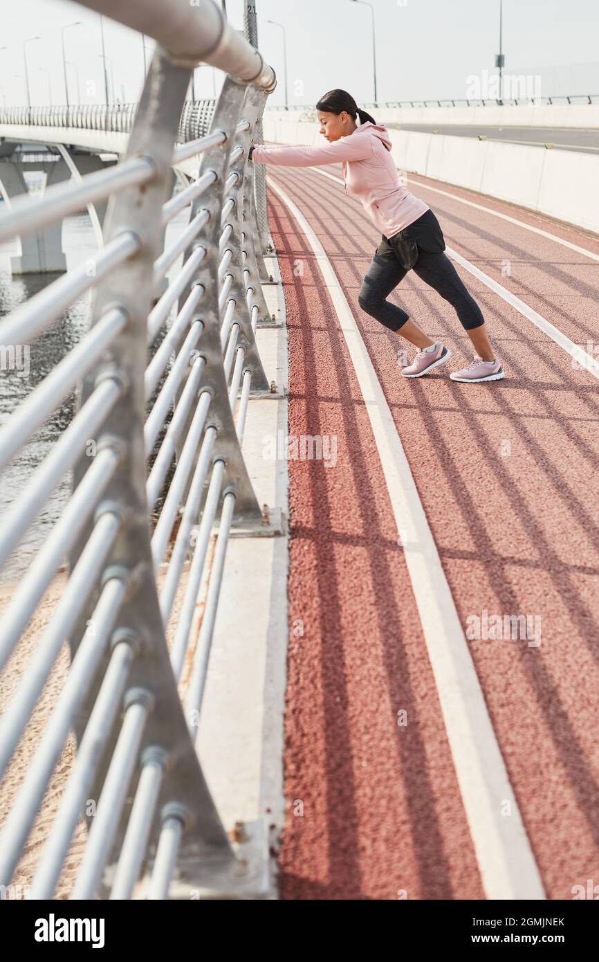 Young woman in sports clothing leaning on the railing doing exercises ...