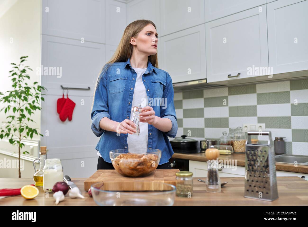 Young woman cooking chicken, marinating with spices black pepper salt ...