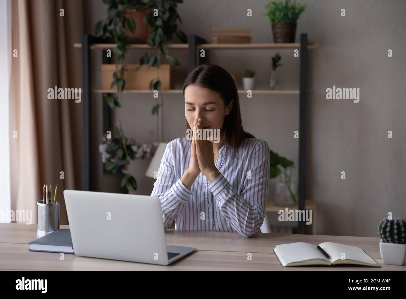 Hopeful religious businesswoman joining hands in prayer, sitting at ...